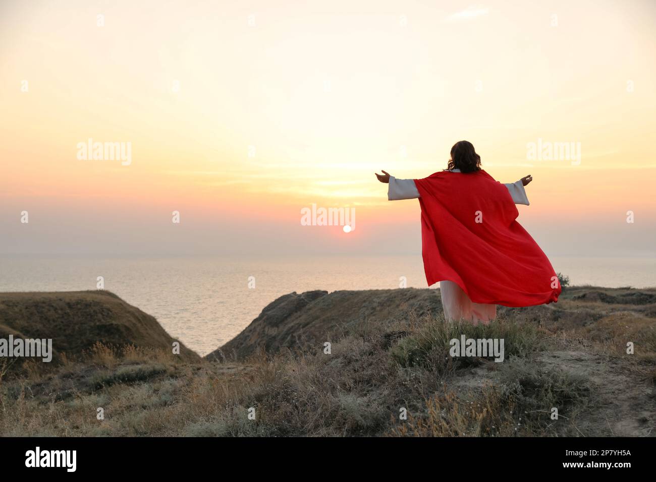 Jesus Christ raising hands on hills at sunset, back view. Space for ...