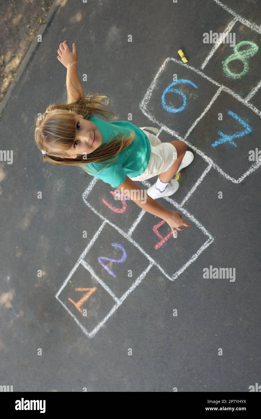 Little girl playing hopscotch drawn with chalk on asphalt outdoors ...