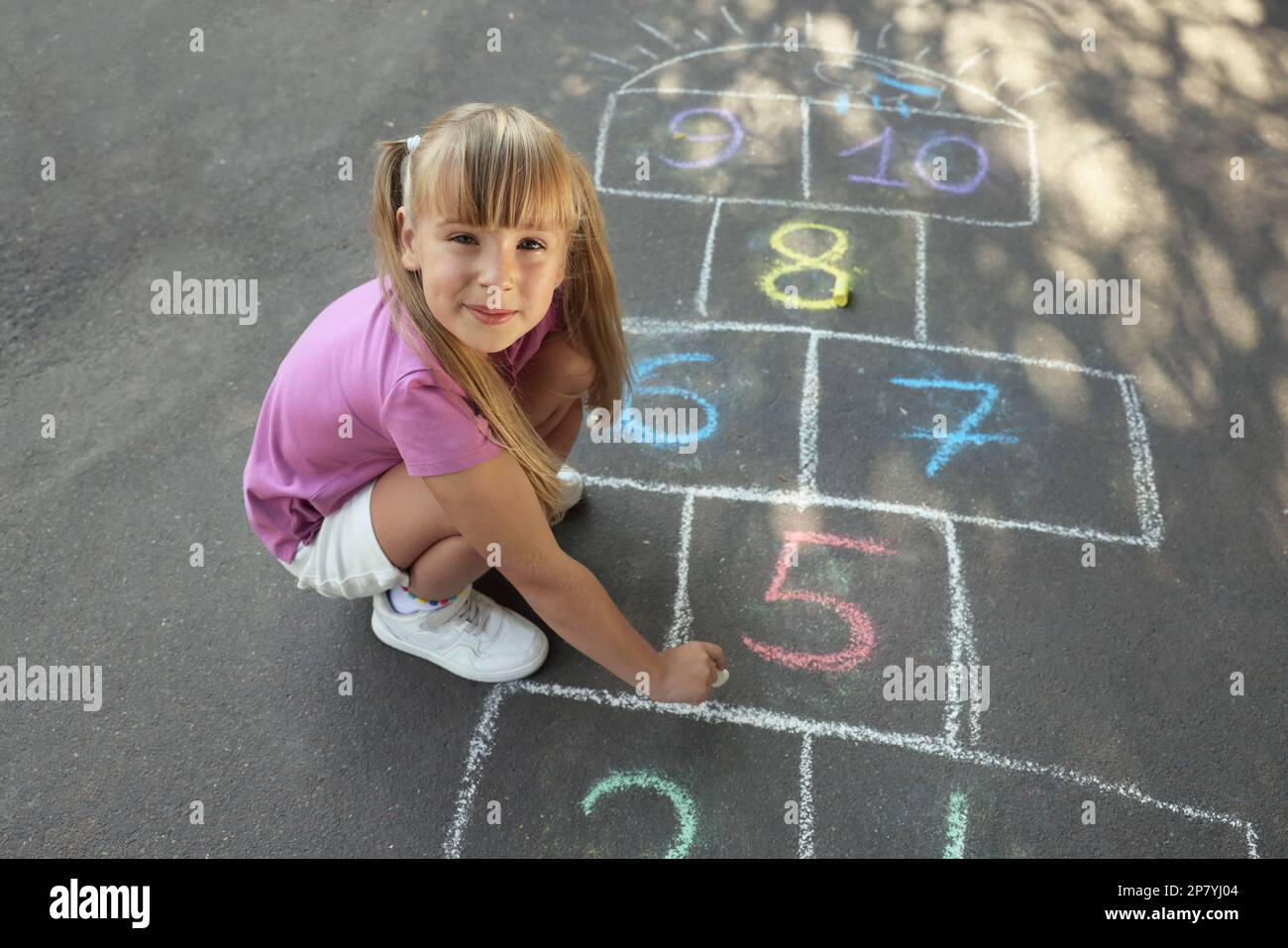 Little girl drawing hopscotch with chalk on asphalt outdoors. Happy ...