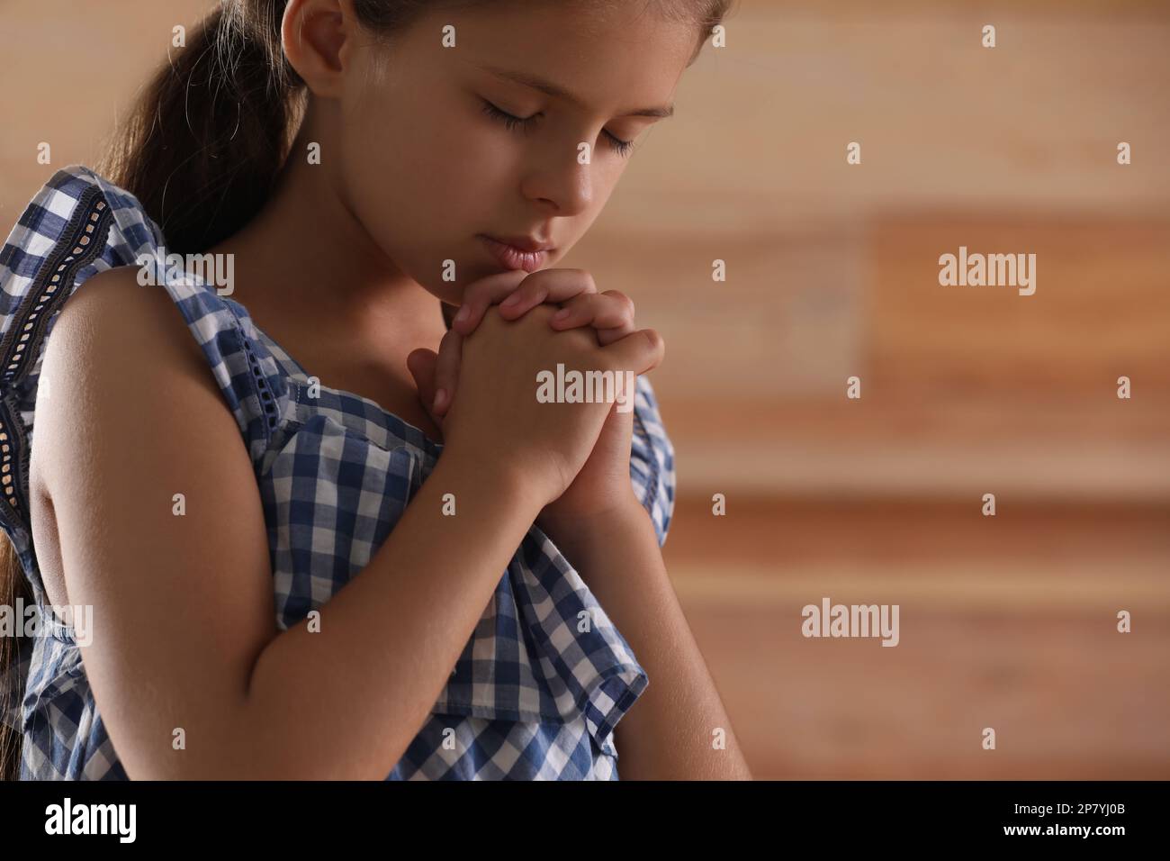 Cute little girl with hands clasped together praying on blurred ...