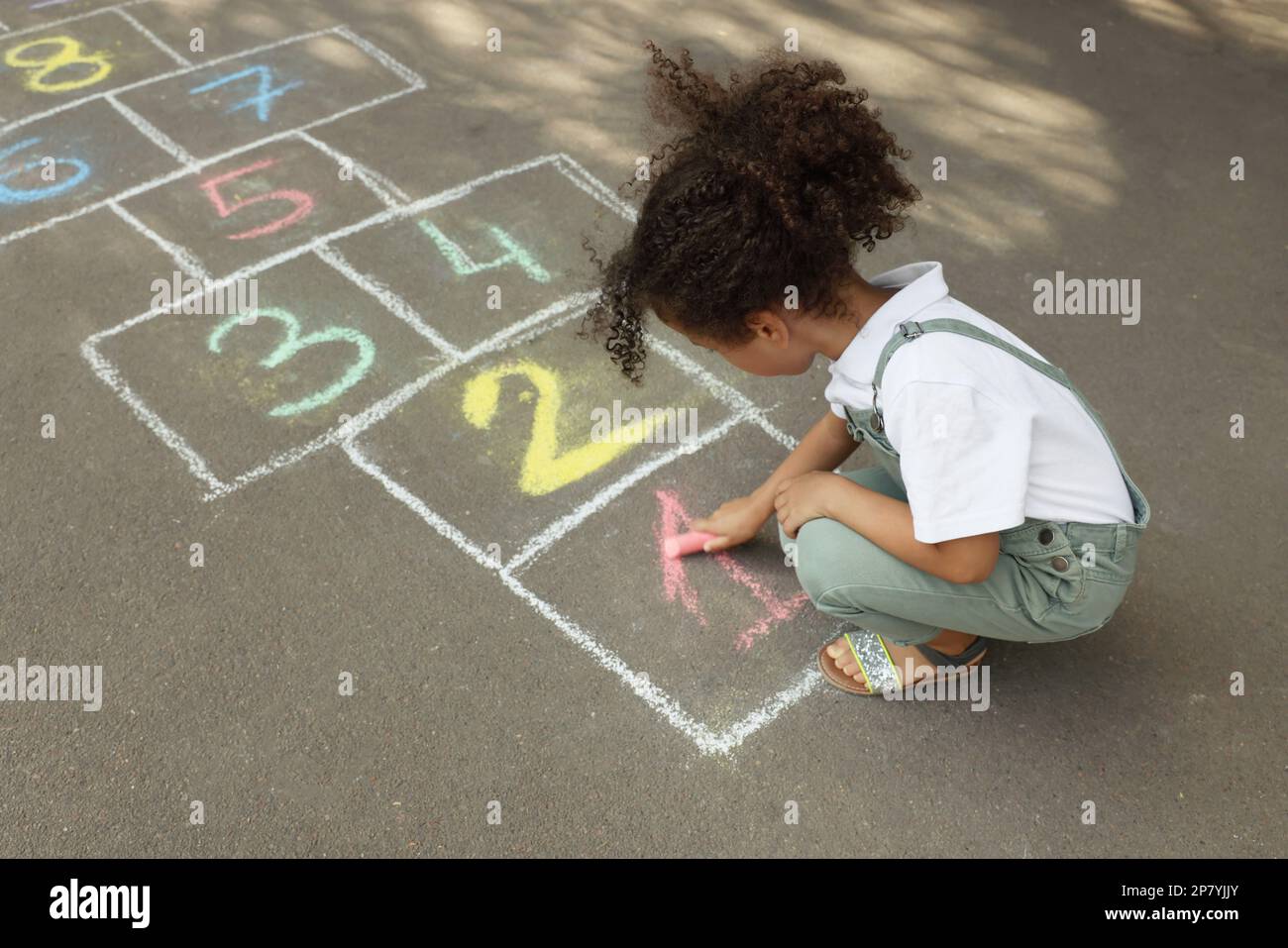 Little African American girl drawing hopscotch with chalk on asphalt ...