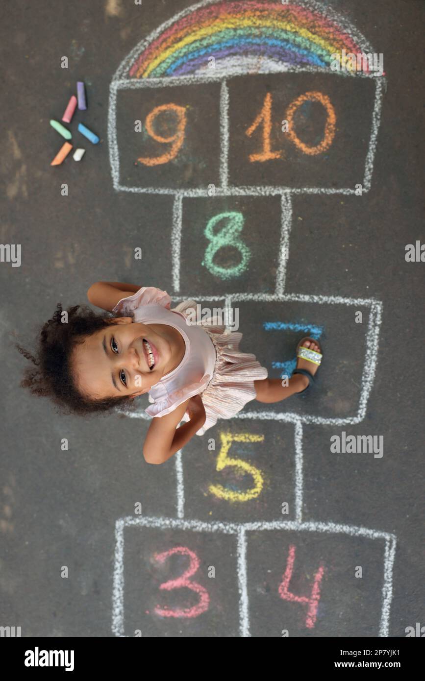 Little African American girl and colorful hopscotch drawn with chalk on ...