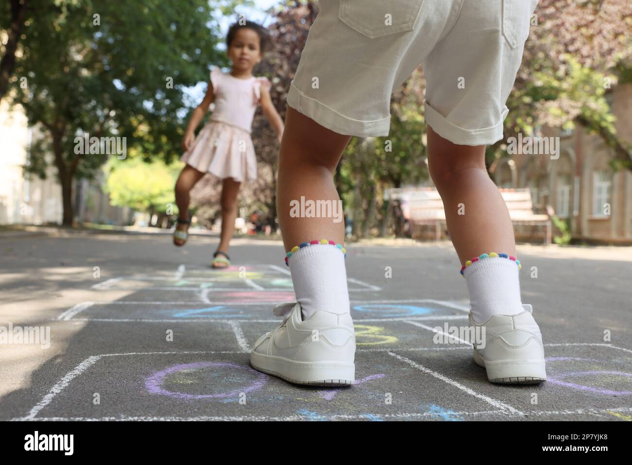 Little children playing hopscotch drawn with chalk on asphalt outdoors ...