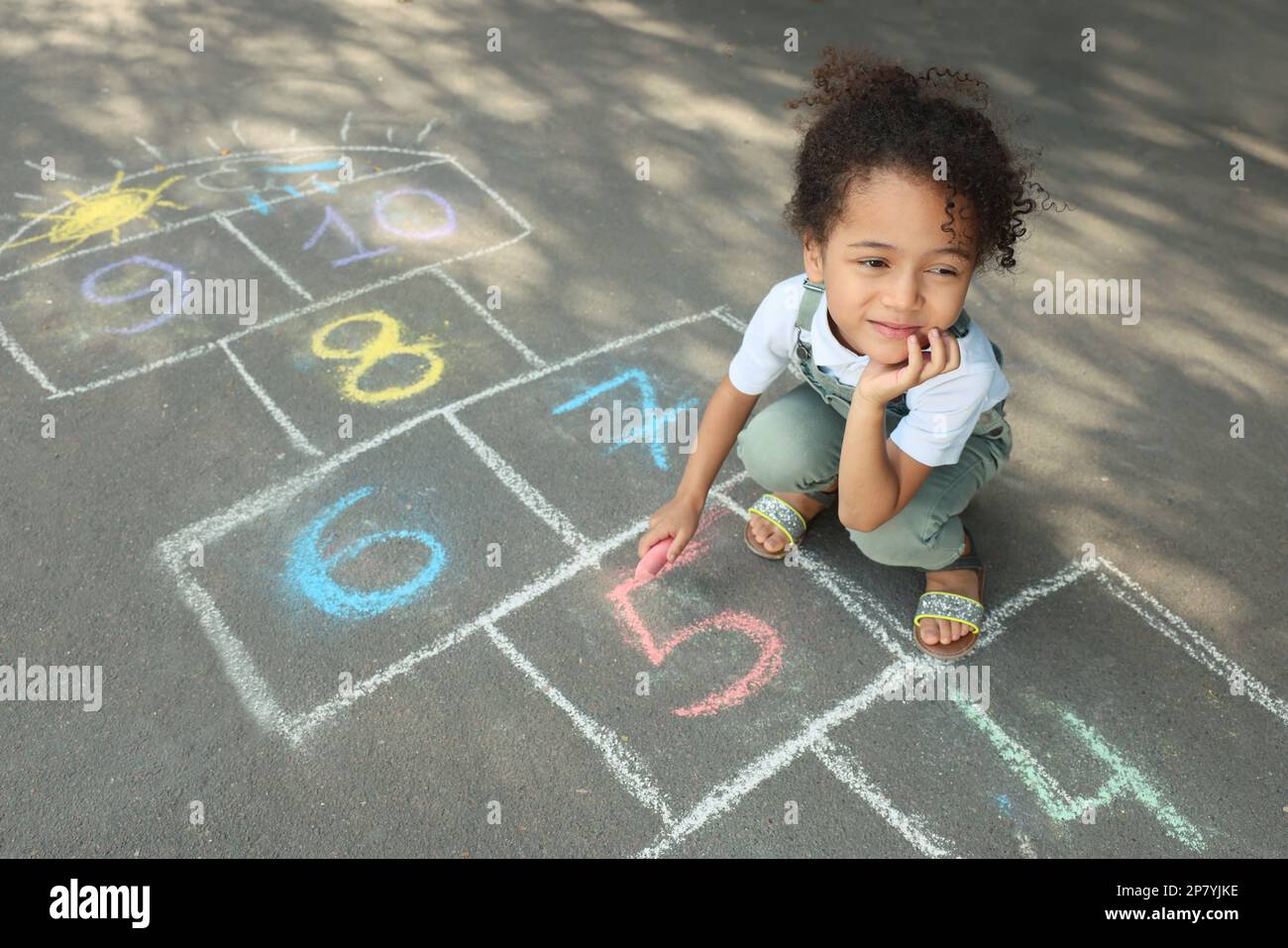 Little African American girl drawing hopscotch with chalk on asphalt ...