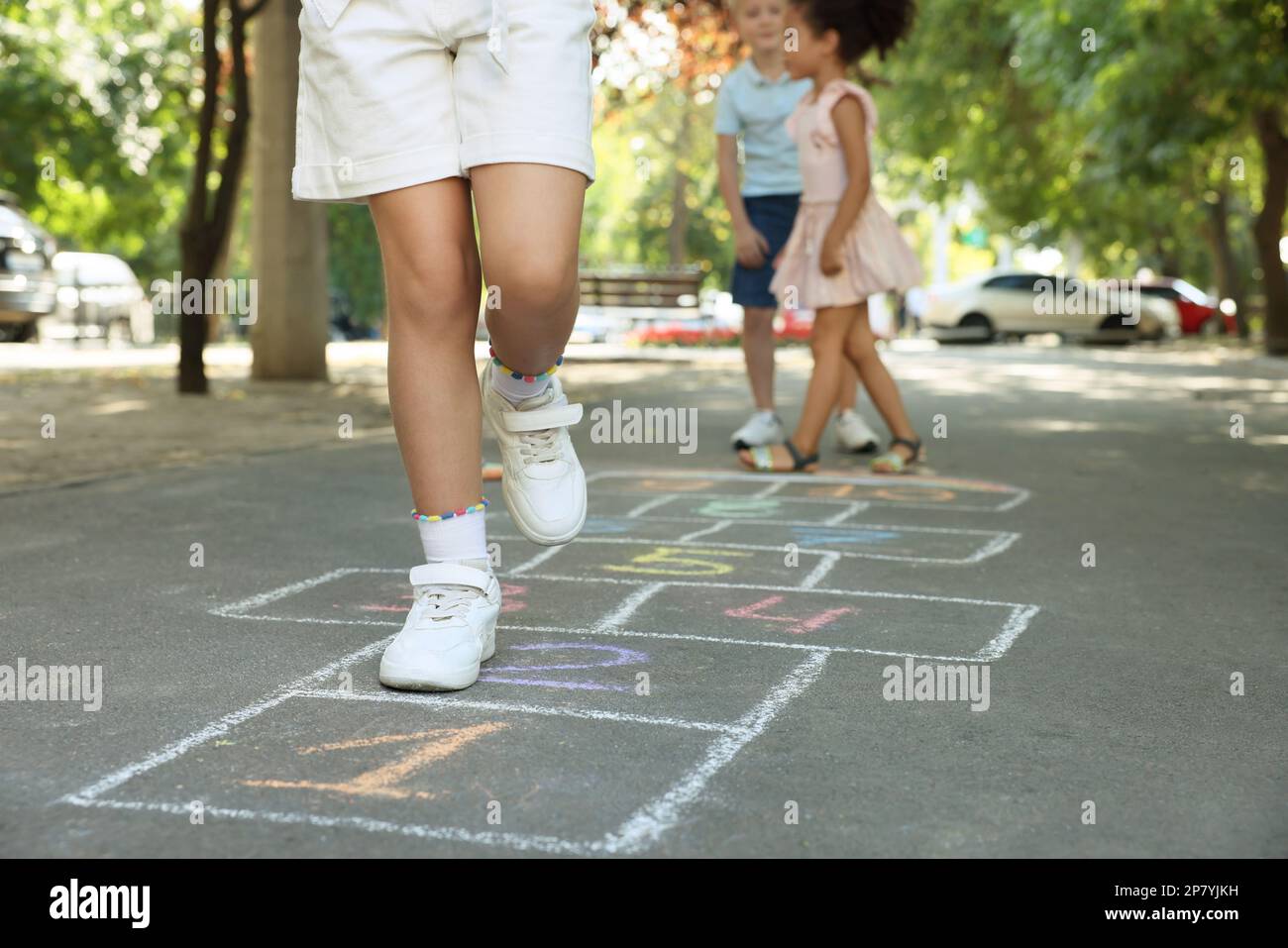 Little children playing hopscotch drawn with chalk on asphalt outdoors ...