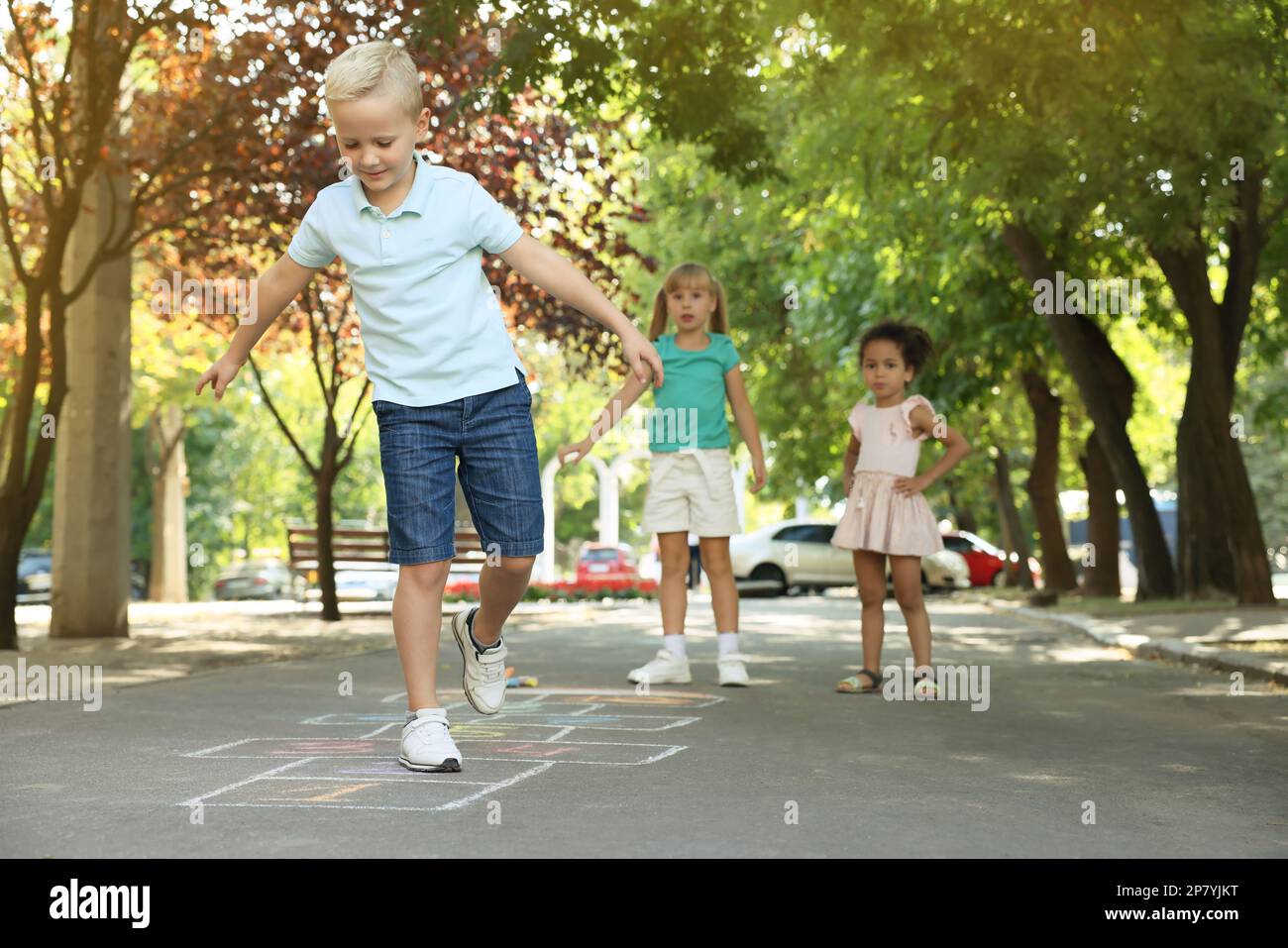 Little children playing hopscotch drawn with chalk on asphalt outdoors ...