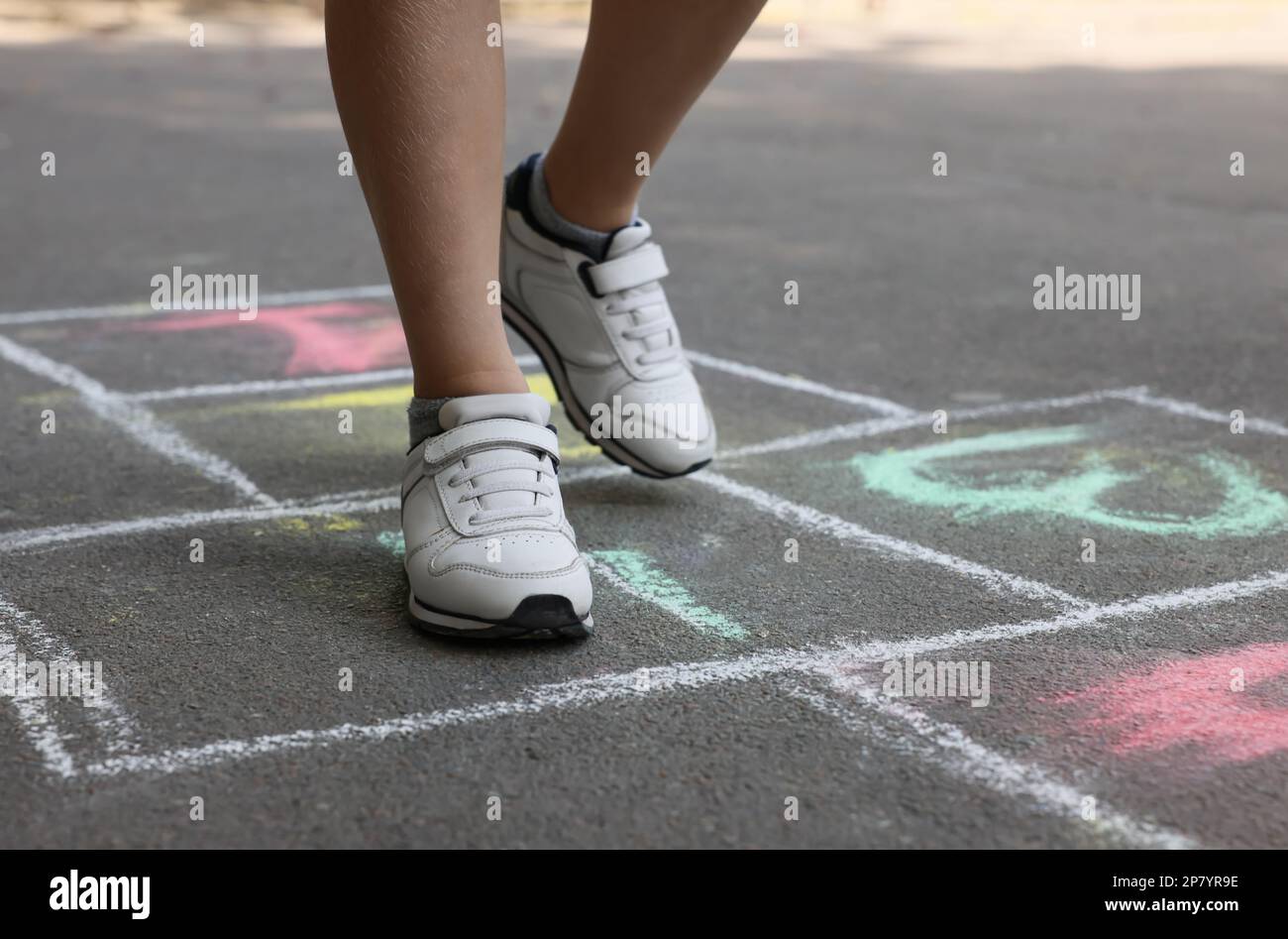 Little child playing hopscotch drawn with chalk on asphalt outdoors ...
