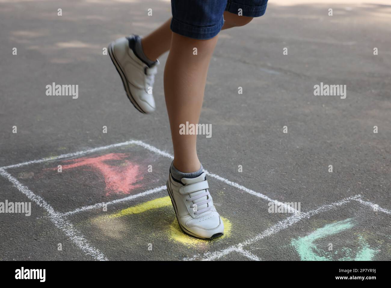Little child playing hopscotch drawn with chalk on asphalt outdoors ...