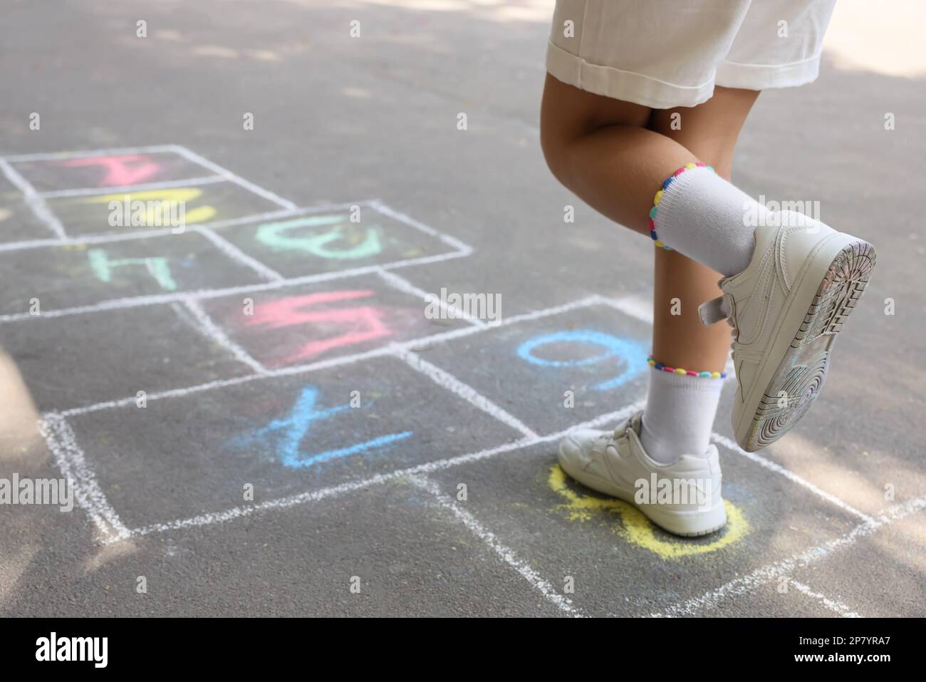 Little child playing hopscotch drawn with chalk on asphalt outdoors ...
