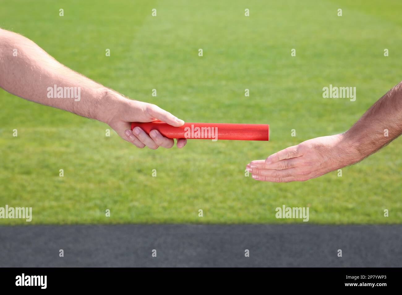 Man passing baton to his partner at stadium, closeup Stock Photo - Alamy
