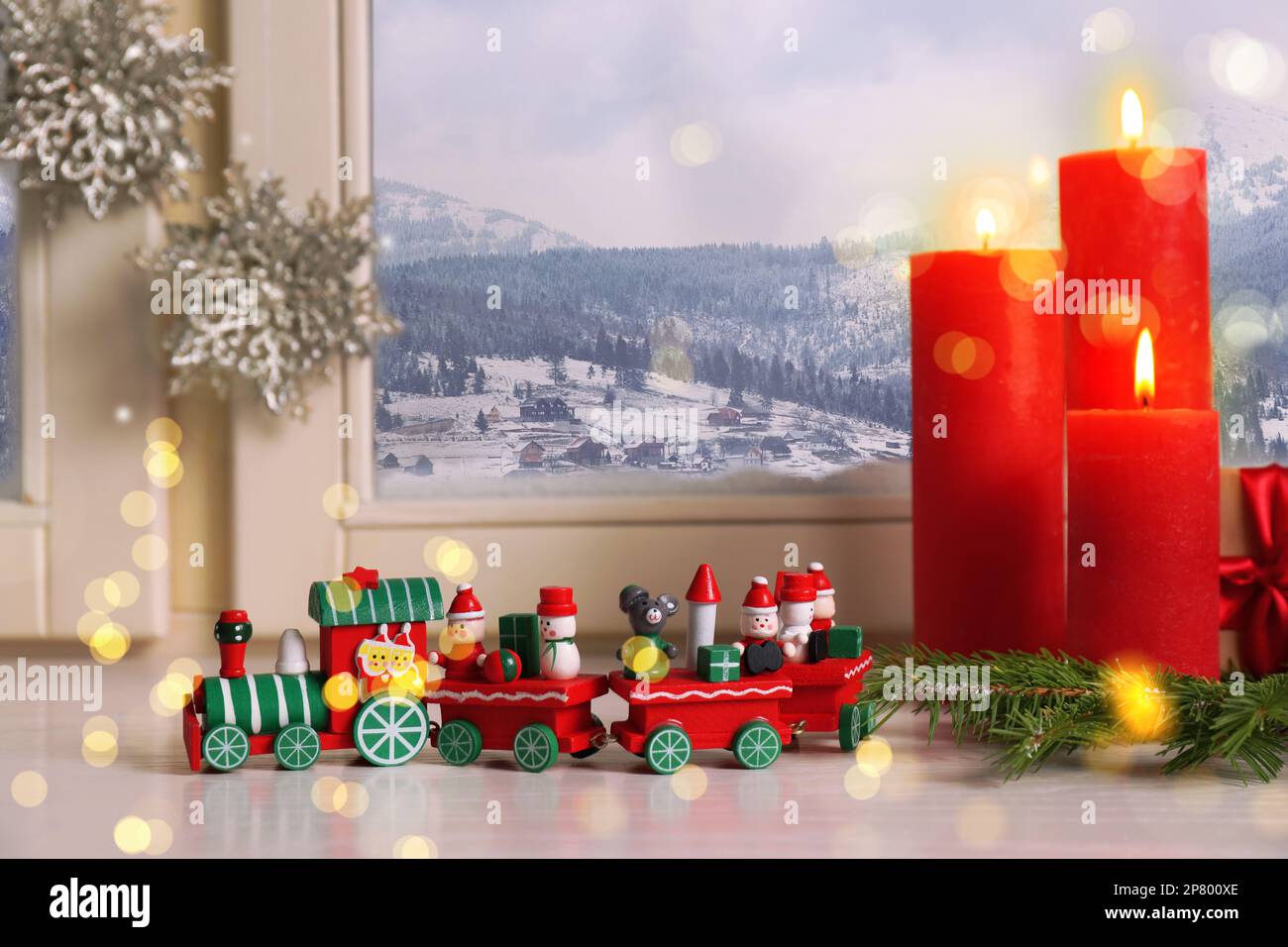 Burning candles and toy train on white window sill indoors. Christmas ...