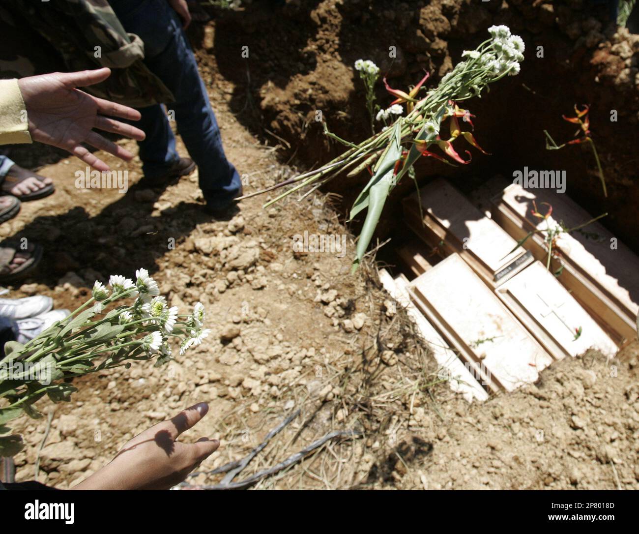 Relatives throw flowers on top of coffins of a family of eight who were ...