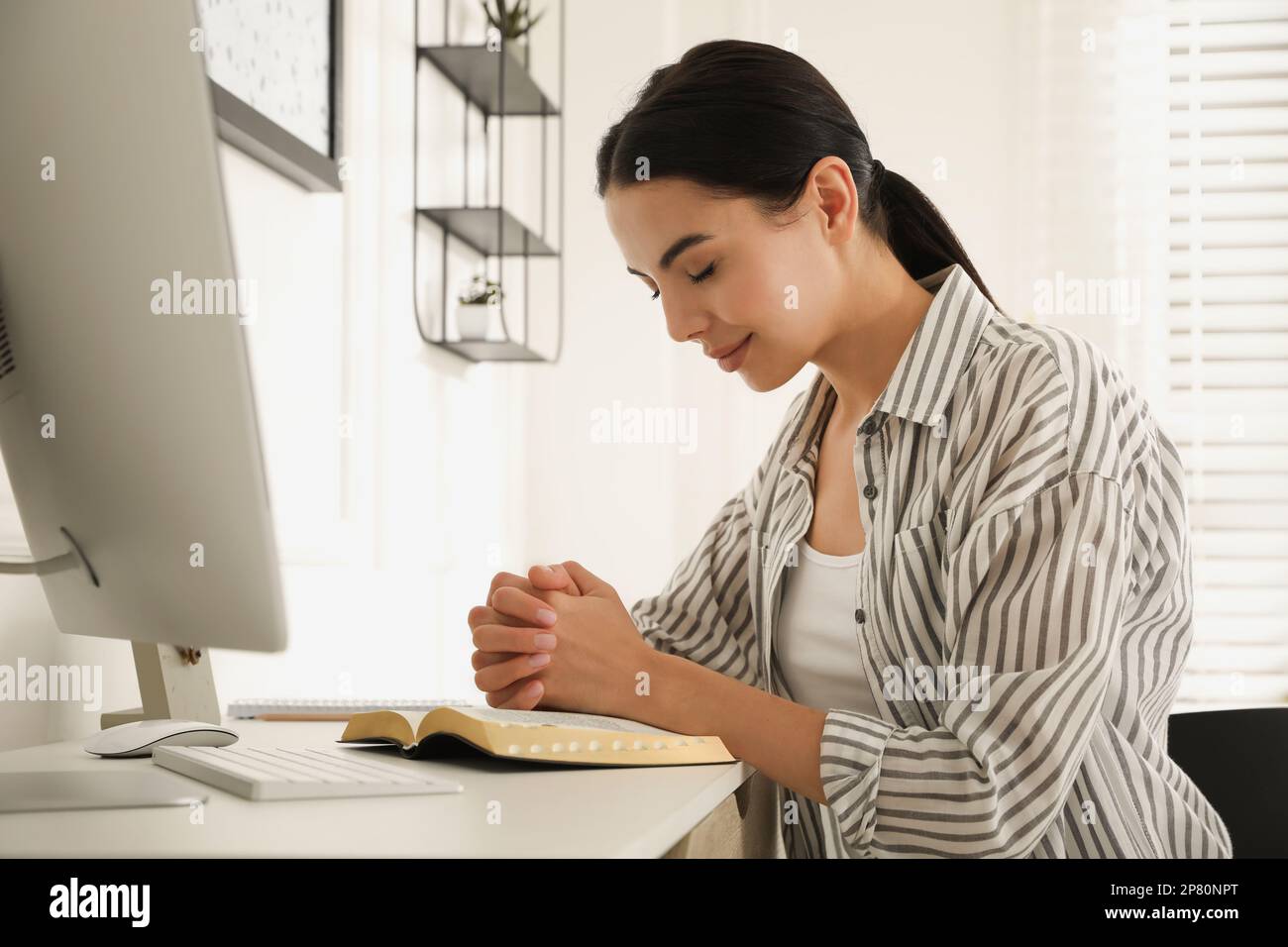 Beautiful young woman praying over Bible at desk Stock Photo - Alamy