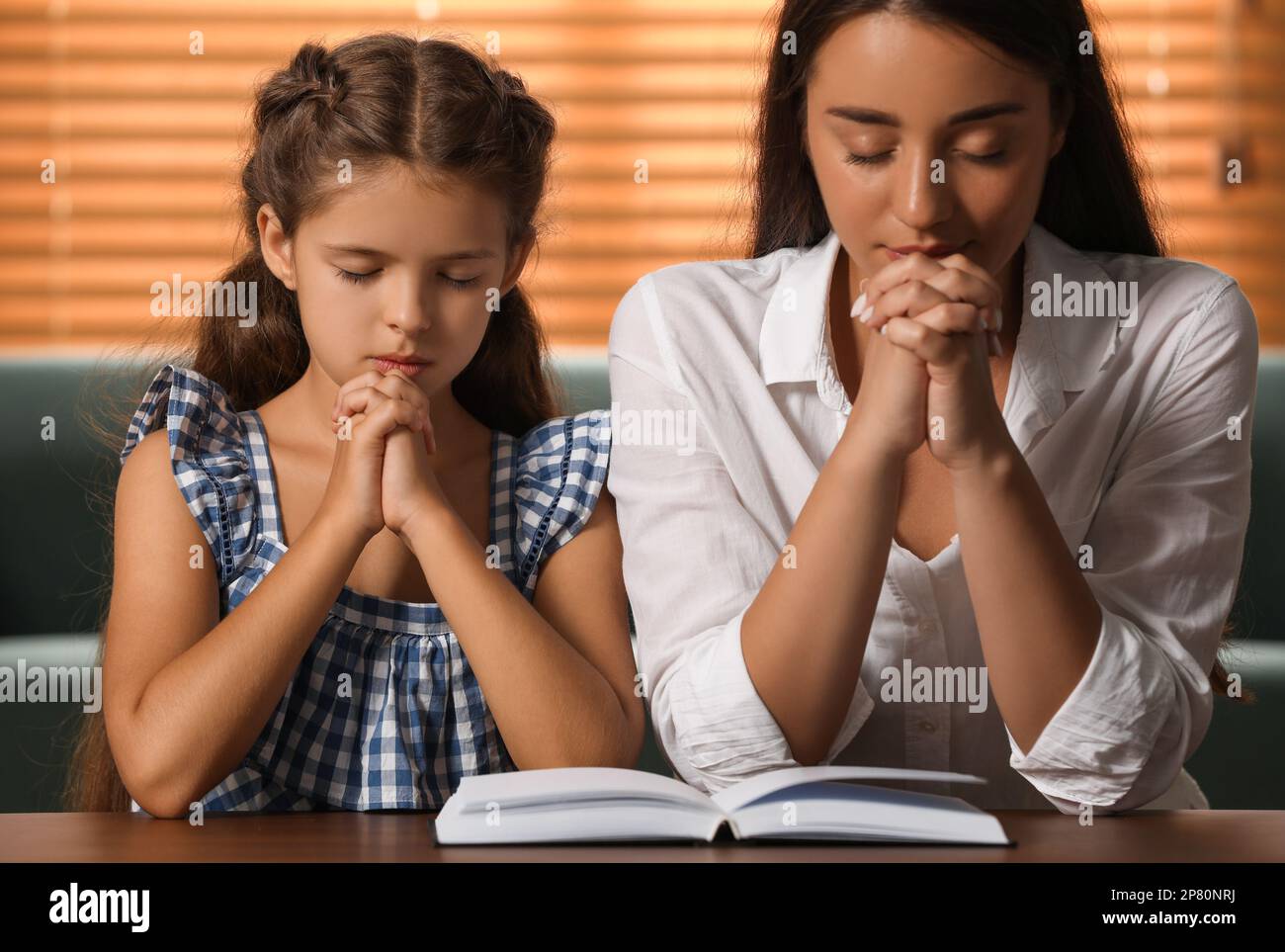 Young woman with her little daughter praying together over Bible at ...