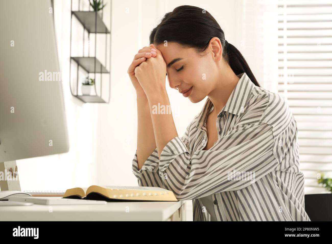 Beautiful young woman praying over Bible at desk Stock Photo - Alamy