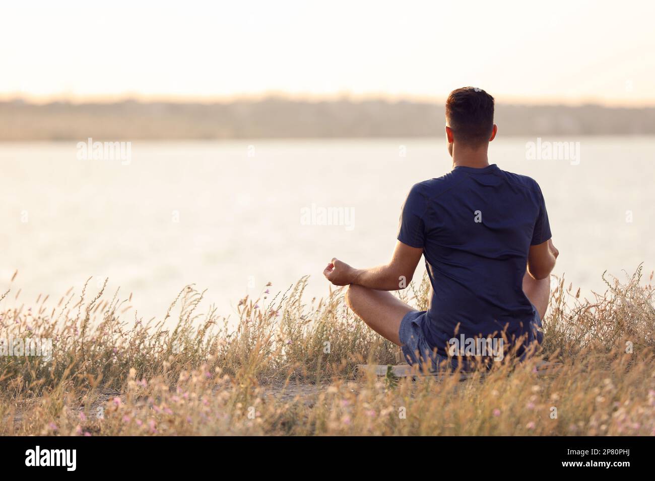 Man meditating near river on sunny day, back view. Space for text Stock ...