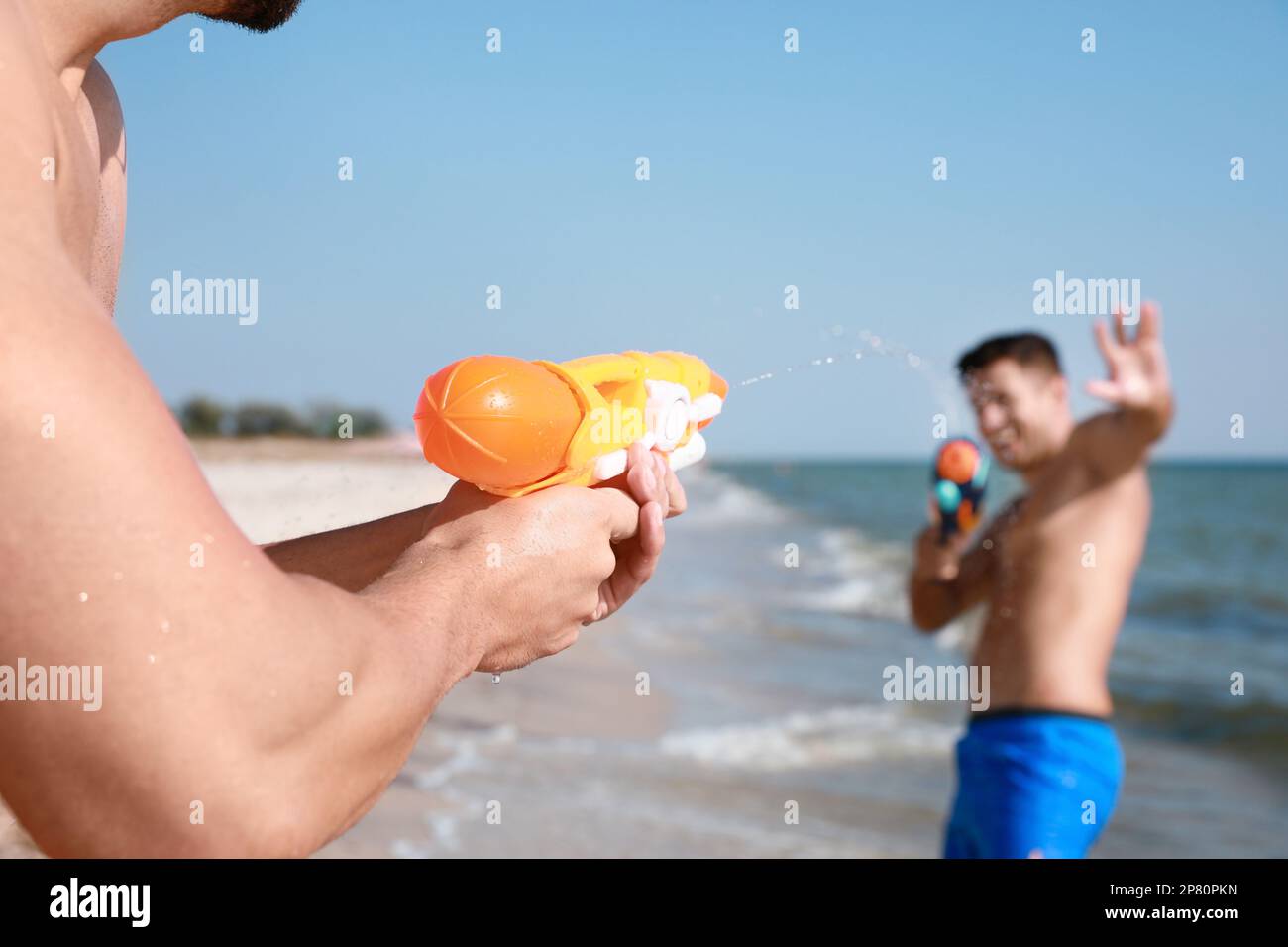 Friends with water guns having fun on beach Stock Photo - Alamy