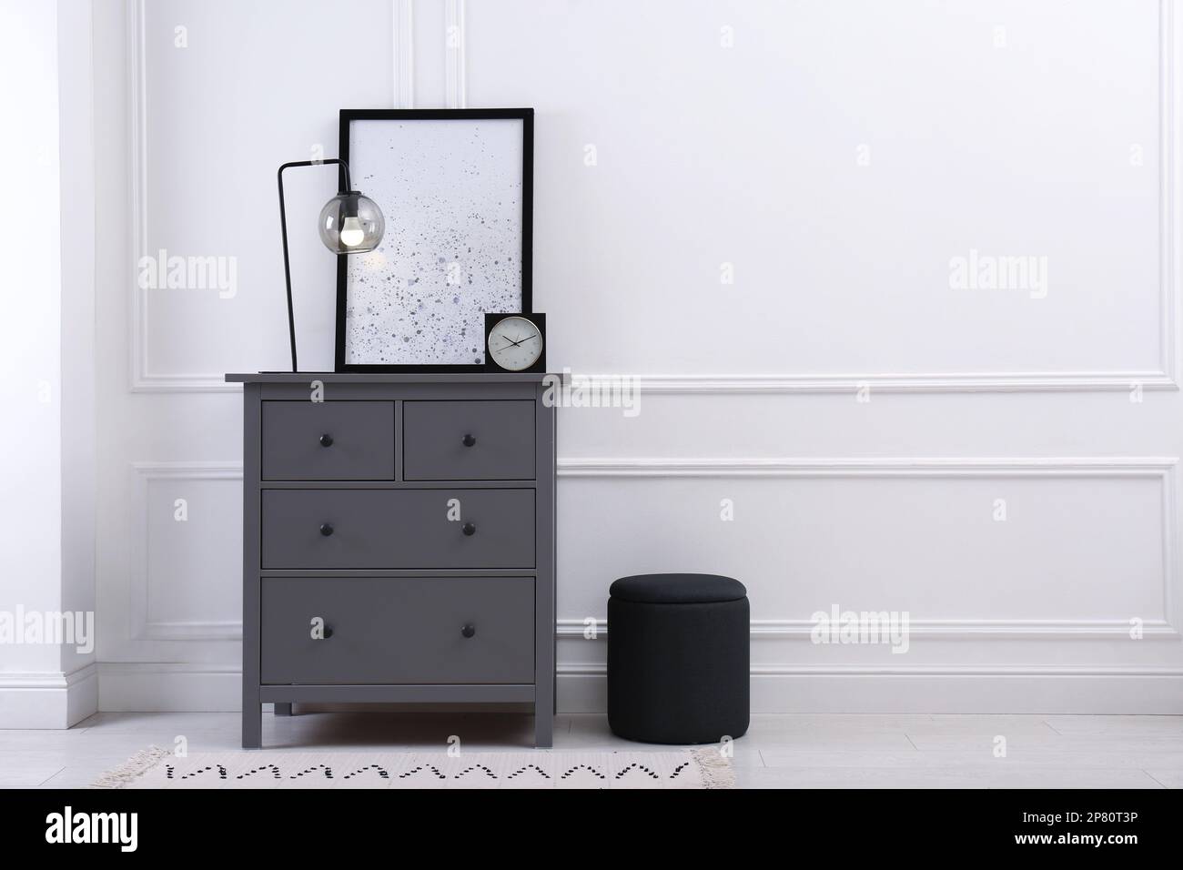 Grey wooden chest of drawers with lamp, clock and picture near white ...