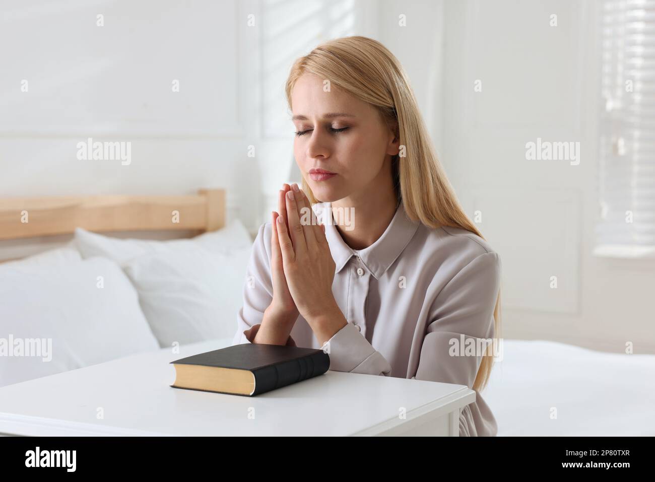 Religious young woman with Bible praying in bedroom Stock Photo - Alamy