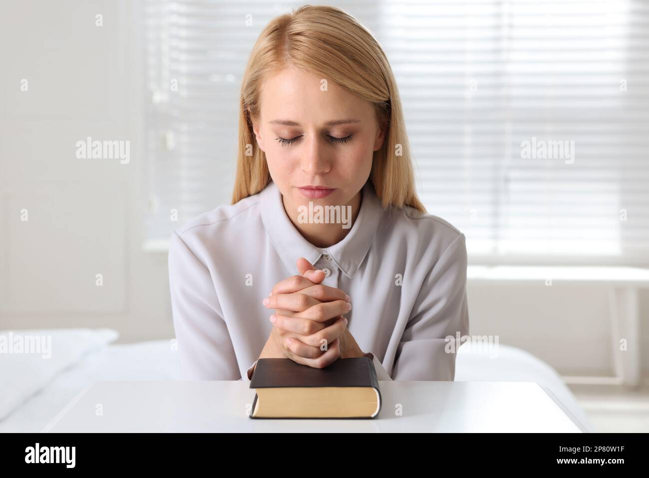 Religious young woman with Bible praying at home Stock Photo - Alamy