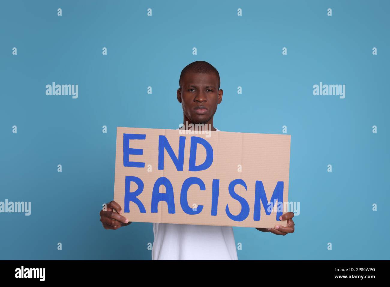 African American man holding sign with phrase End Racism on light blue ...