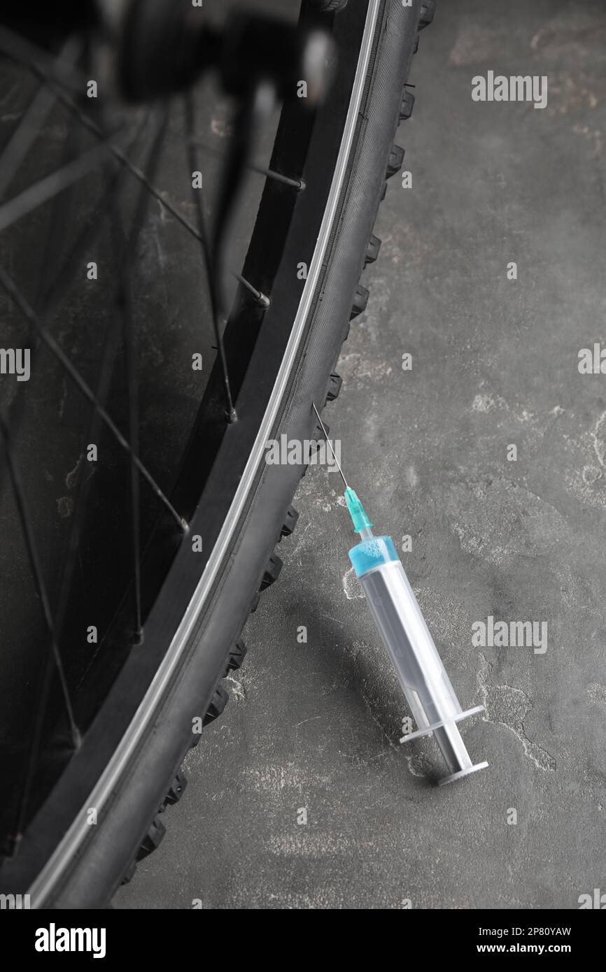 Bike wheel with syringe on grey background, closeup. Using doping in ...