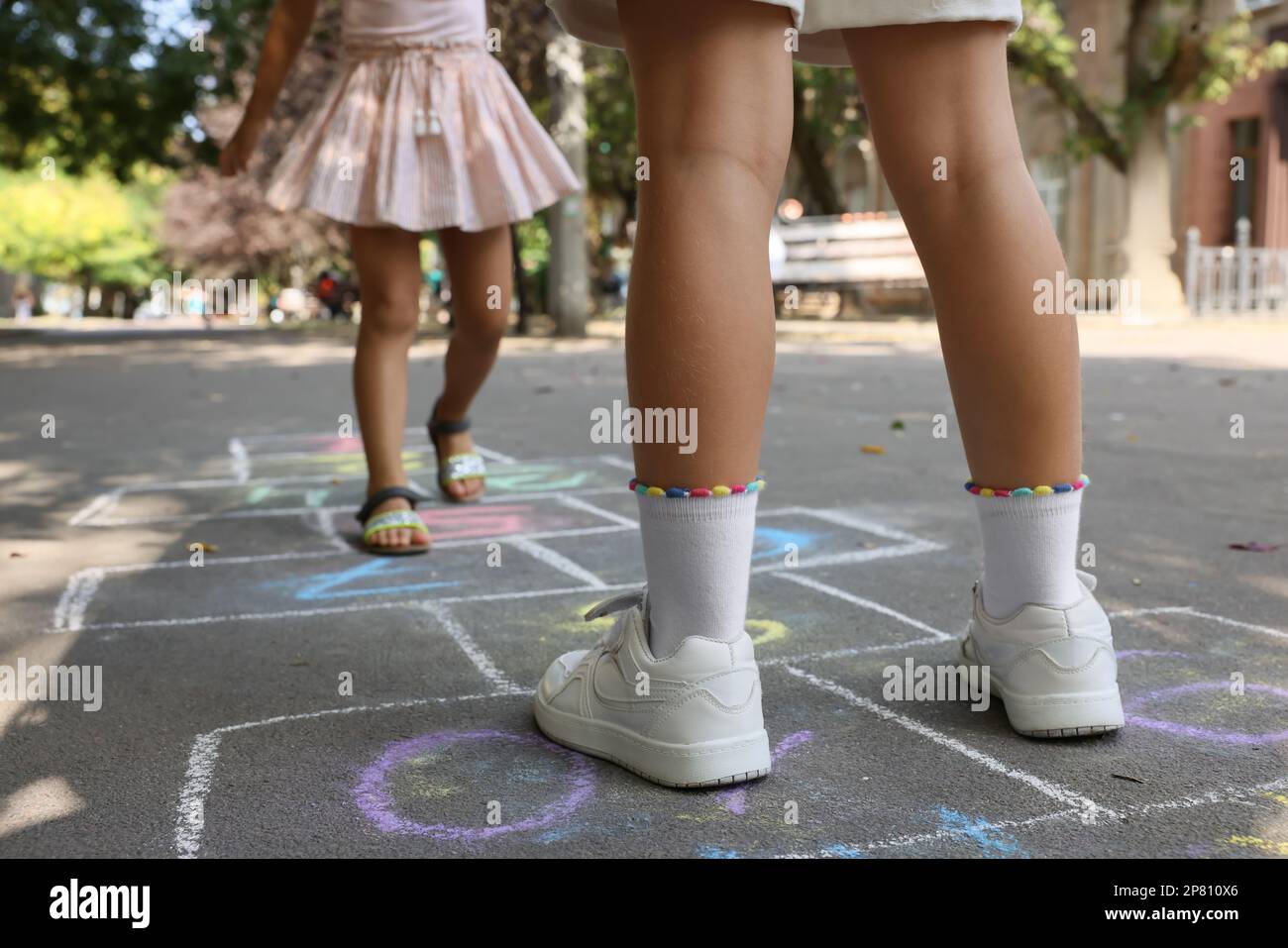 Little children playing hopscotch drawn with chalk on asphalt outdoors ...