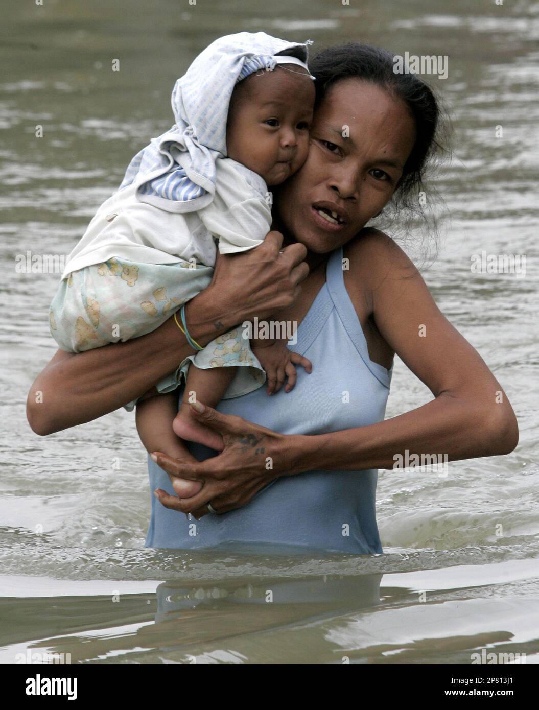 A mother cuddles her child while wading through floodwaters in Taytay ...