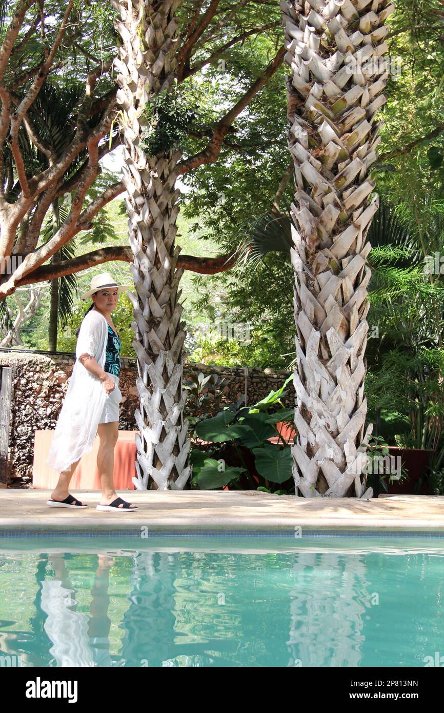 Latin adult woman walks next to a pool, she feels relaxed, fulfilled ...