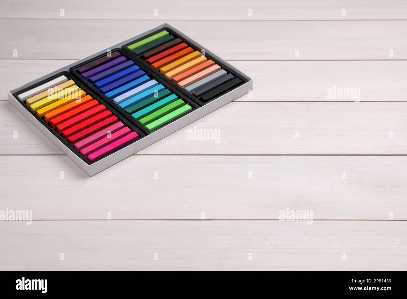 Set of colorful pastels in box on white wooden table, space for text ...