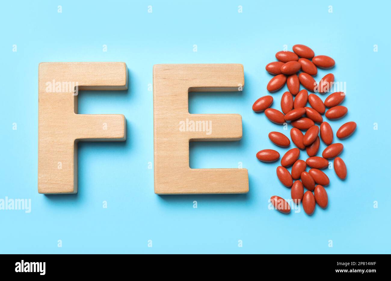 Wooden letters FE and pills on light blue background, flat lay. Anemia ...