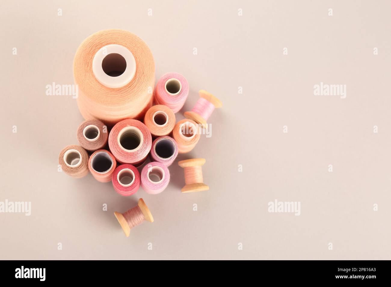 Different shades of pink sewing threads on light background, flat lay ...