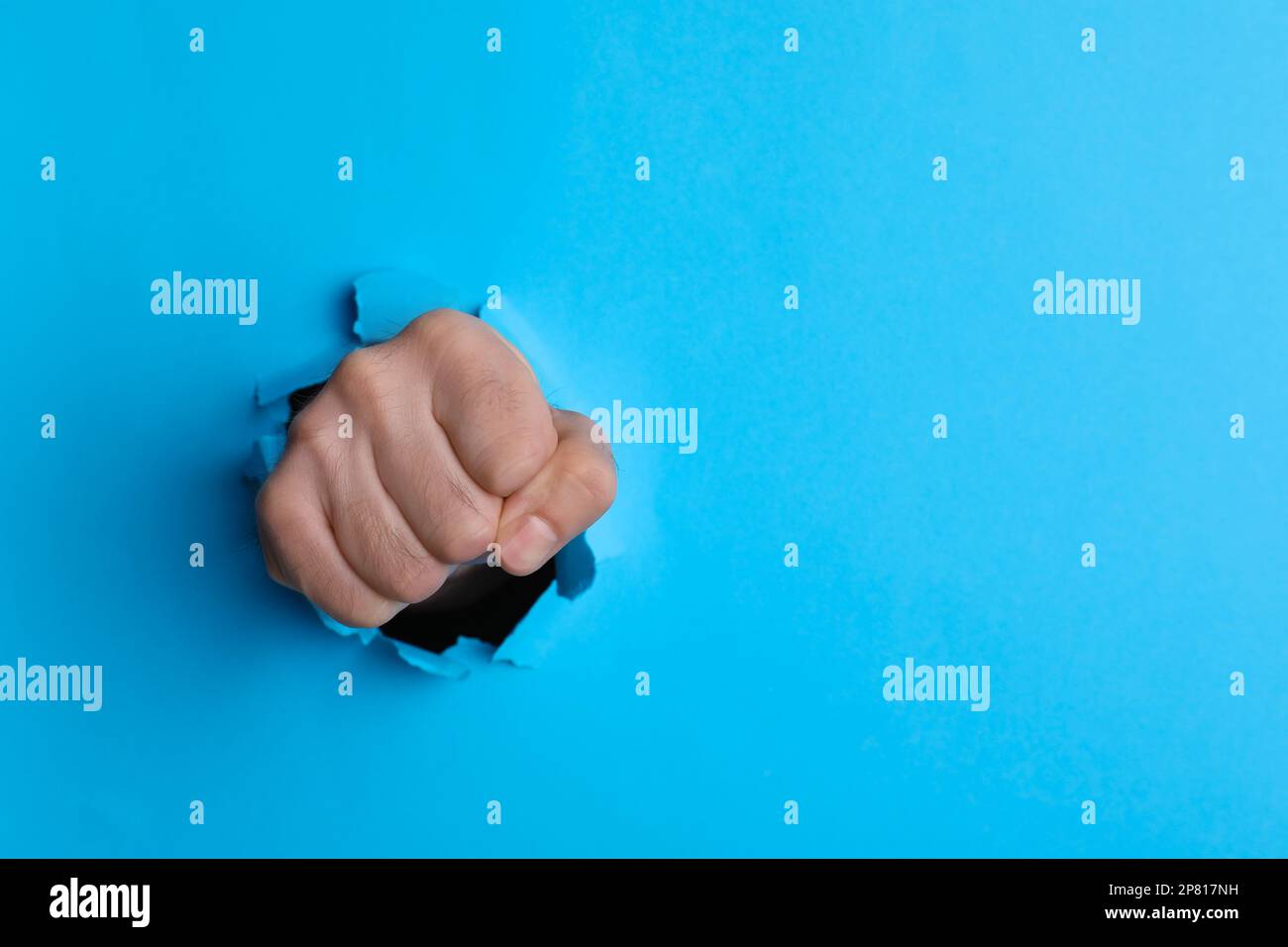 Man breaking through light blue paper with fist, closeup. Space for ...