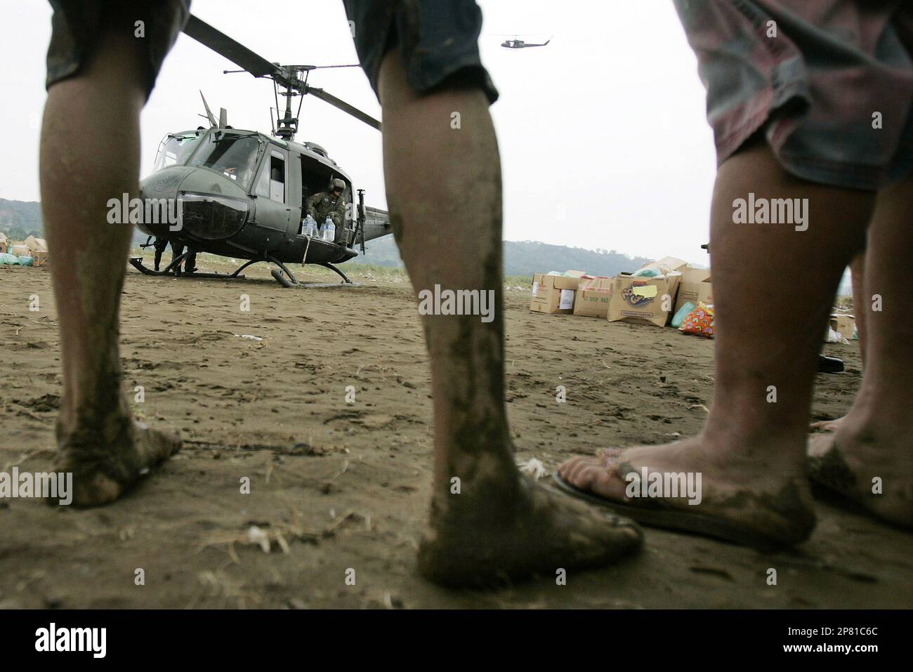 Flood victims wait as a military helicopter delivers relief goods at a ...