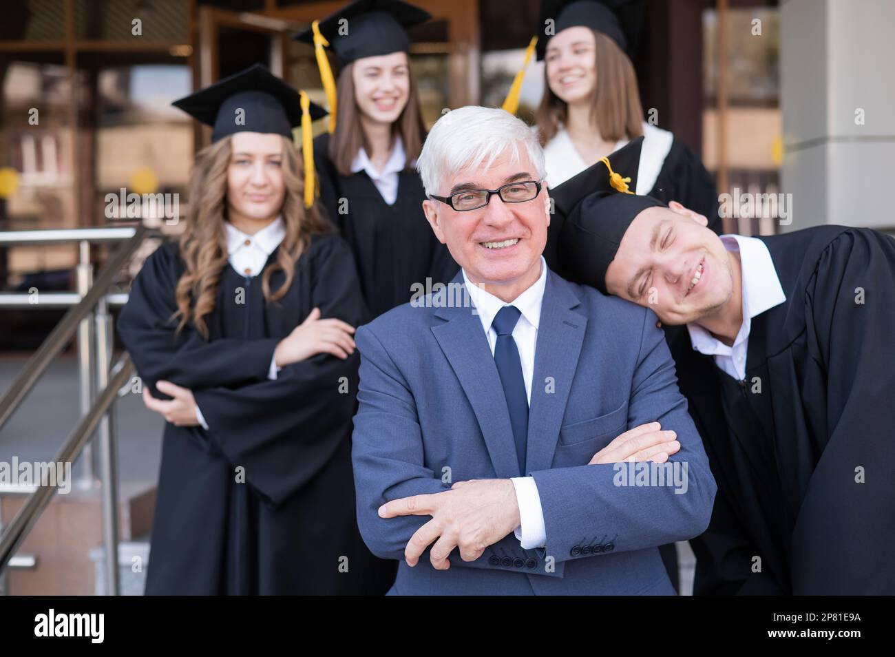 A gray-haired male teacher congratulates students on their graduation ...