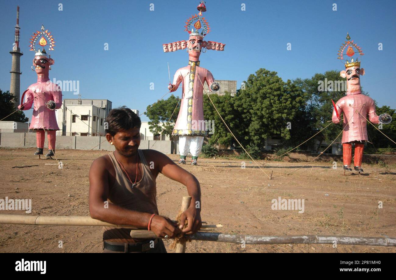A worker erects a fence as effigies of demon king Ravana, center, his ...