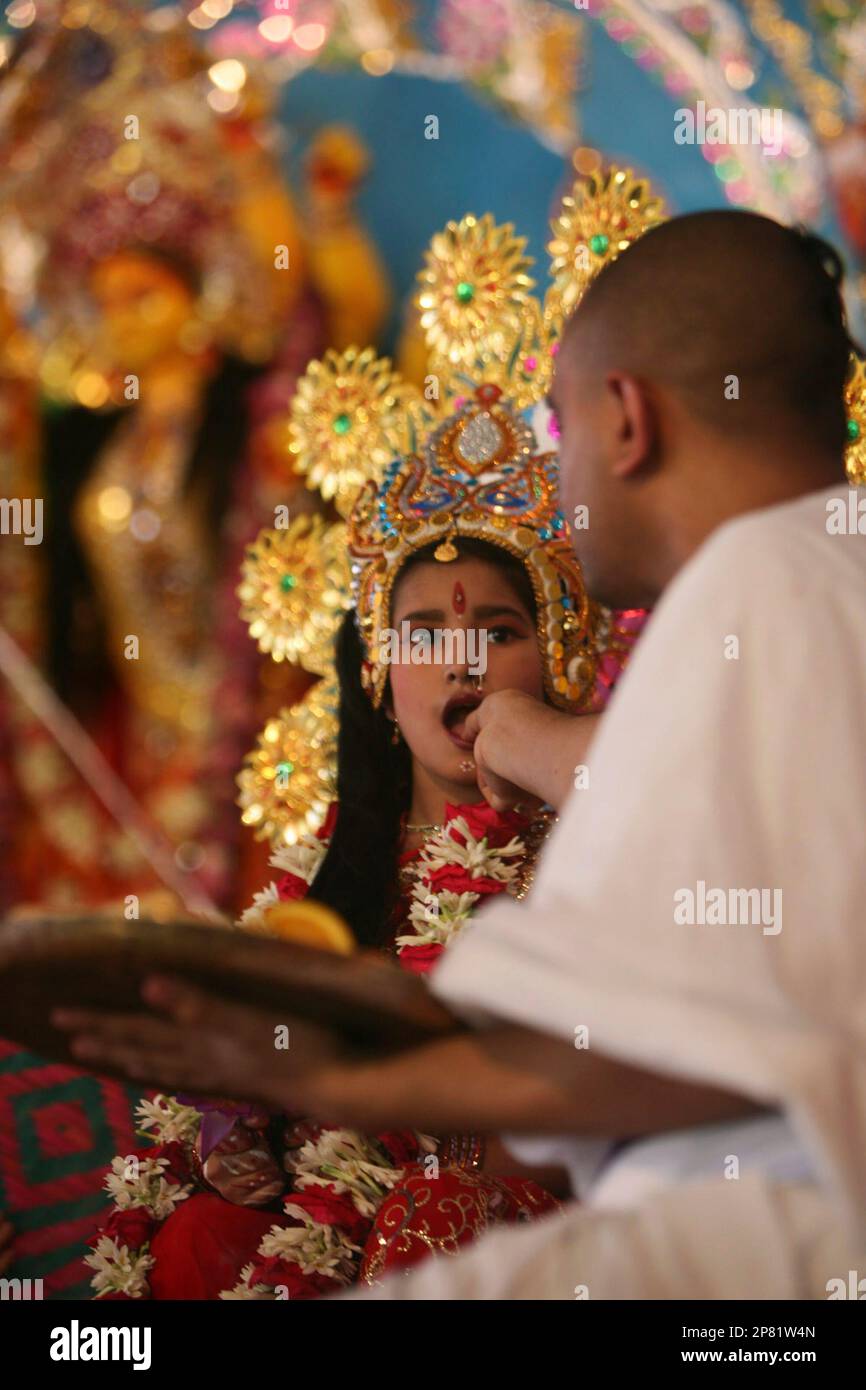 A priest offers sweets to Modhumonjuri, left, dressed as Kumari, or ...