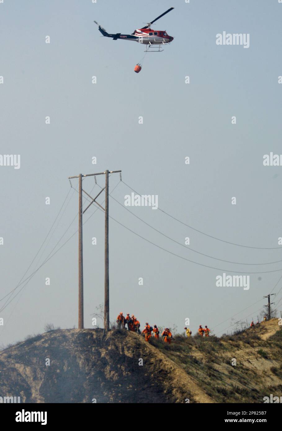 A water-dropping helicopter passes overhead as an inmate hand crew ...