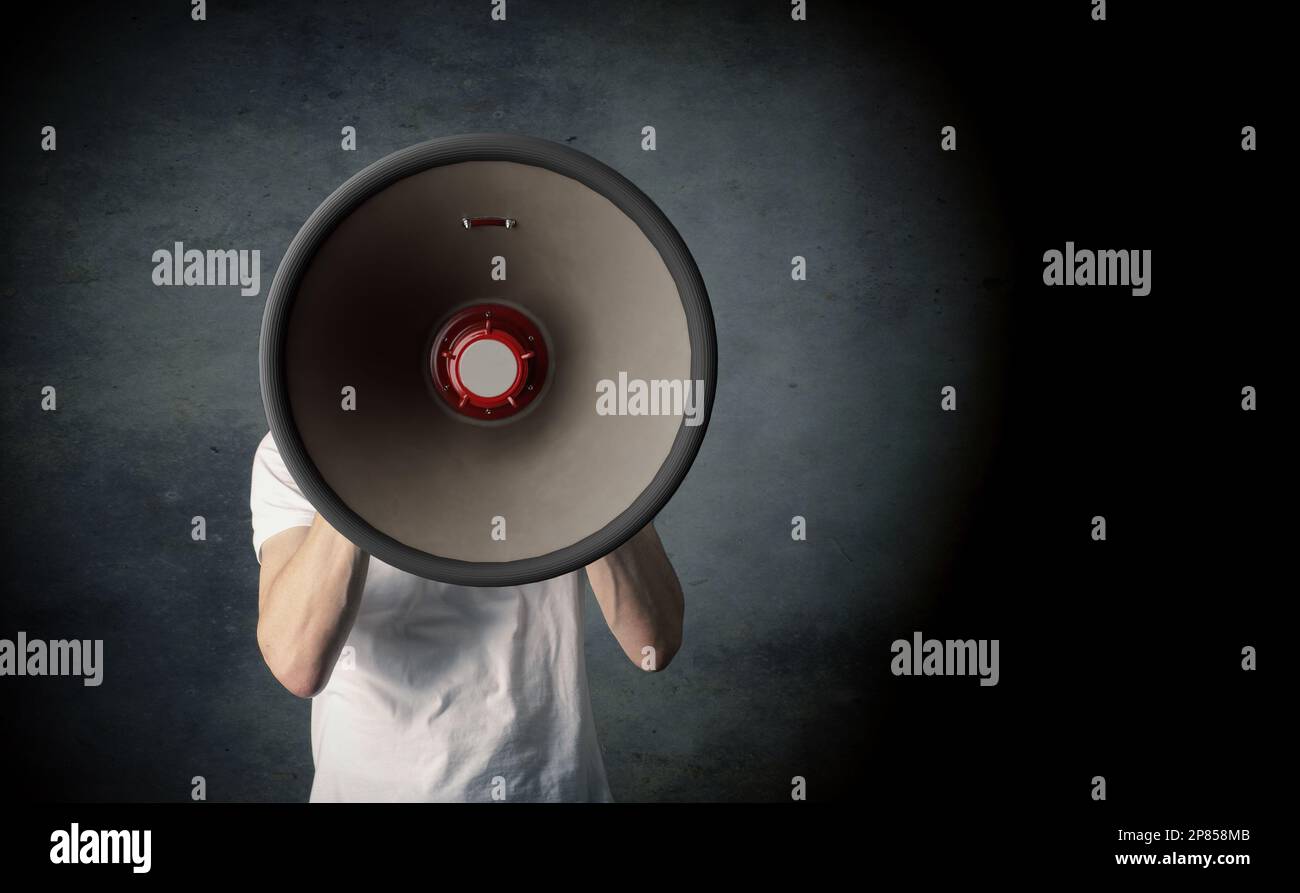 Young man holding a big megaphone, speaking loud concept on a dark ...