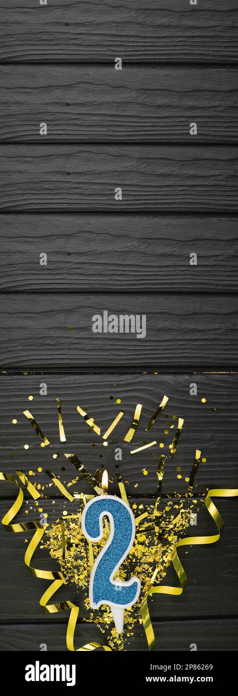 Number 2 blue celebration candle and gold confetti on dark wooden ...