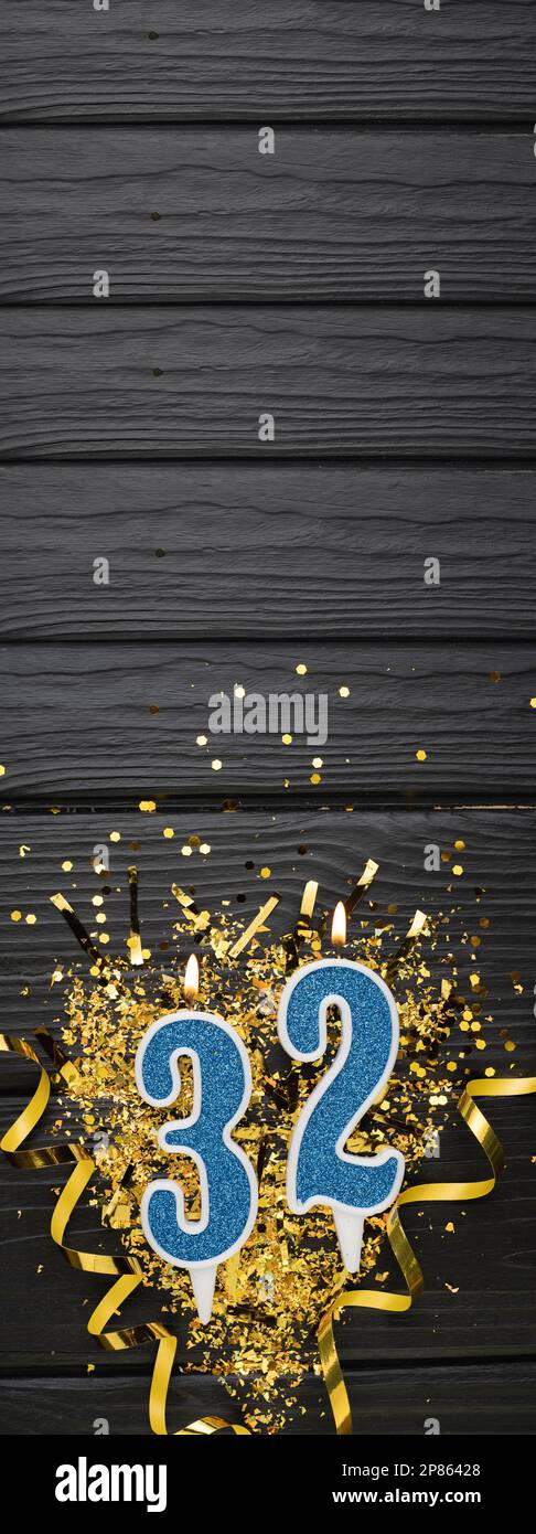 Number 32 blue celebration candle and gold confetti on dark wooden ...