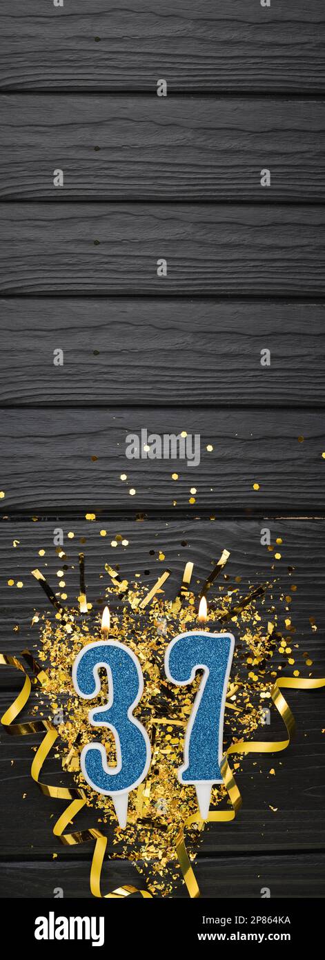 Number 37 blue celebration candle and gold confetti on dark wooden ...