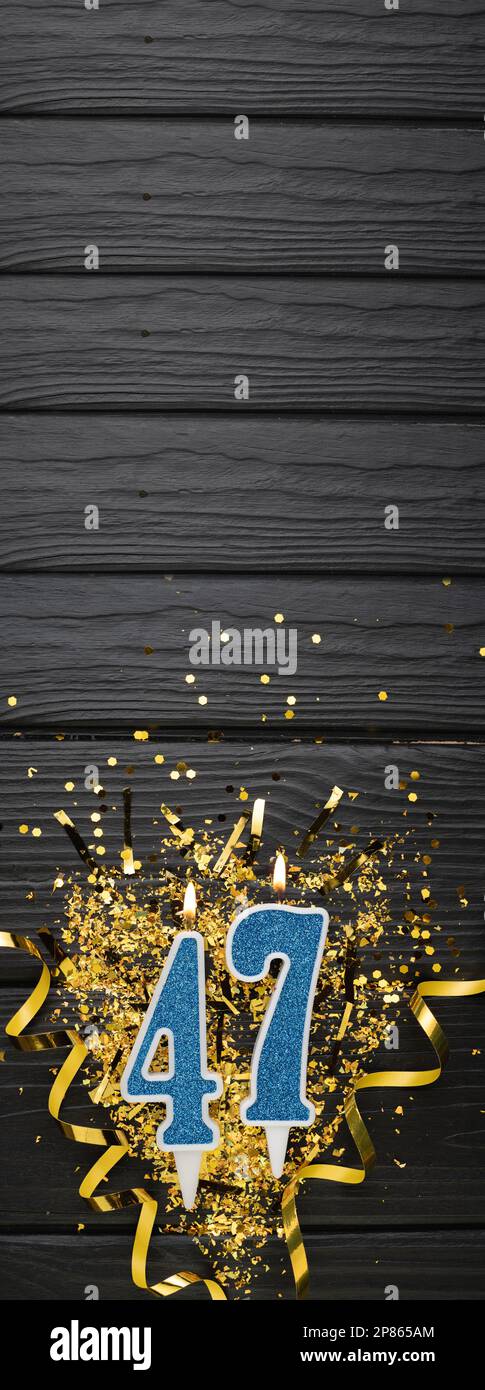Number 47 blue celebration candle and gold confetti on dark wooden ...