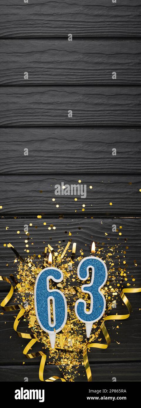 Number 63 blue celebration candle and gold confetti on dark wooden ...
