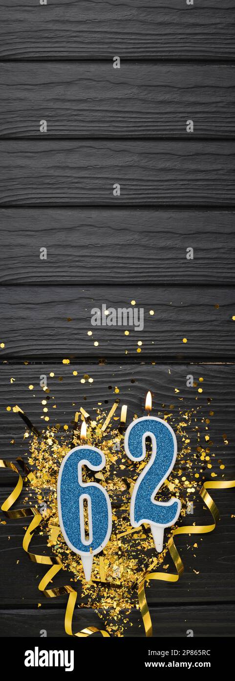 Number 62 blue celebration candle and gold confetti on dark wooden ...