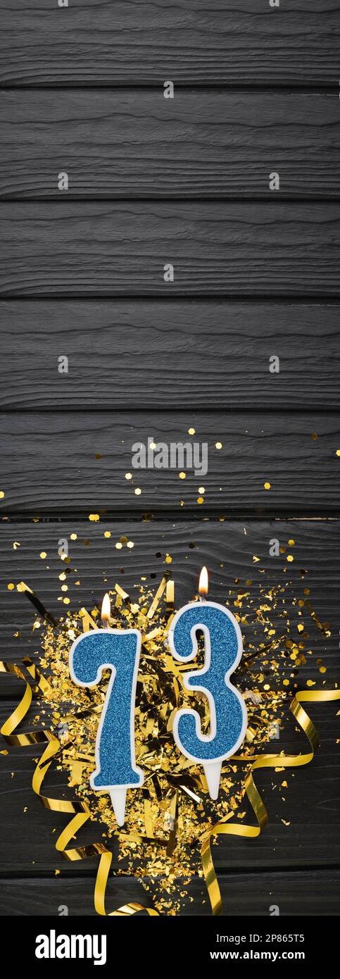 Number 73 blue celebration candle and gold confetti on dark wooden ...