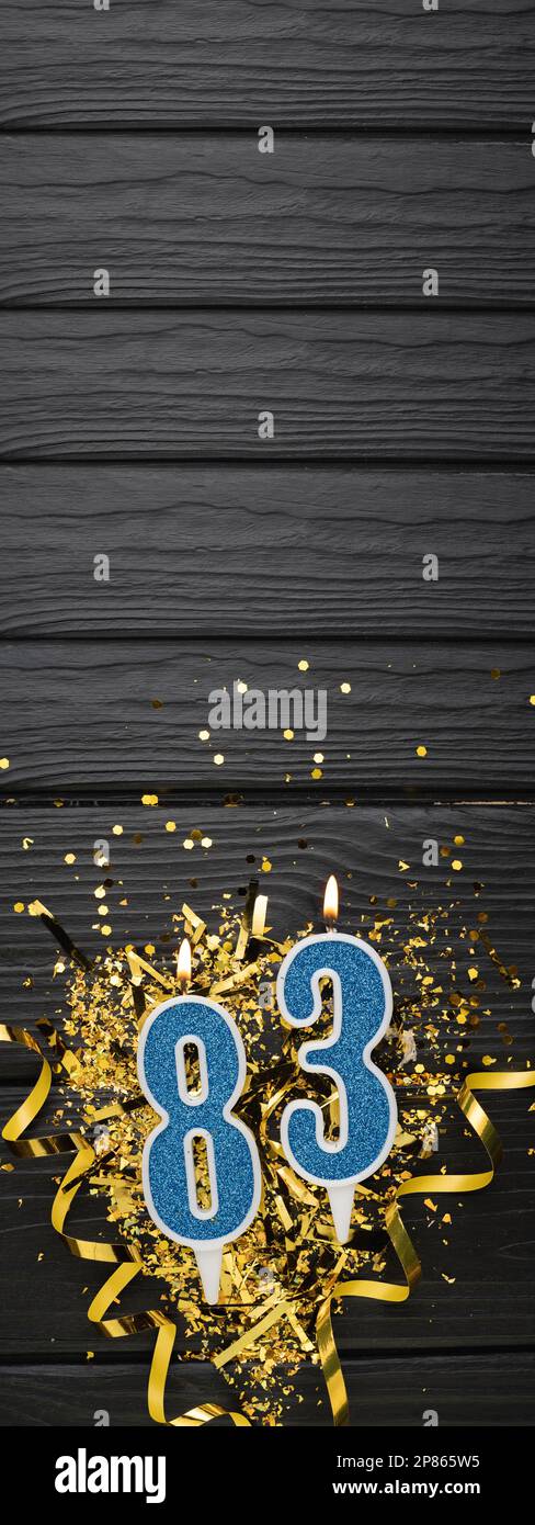 Number 83 blue celebration candle and gold confetti on dark wooden ...