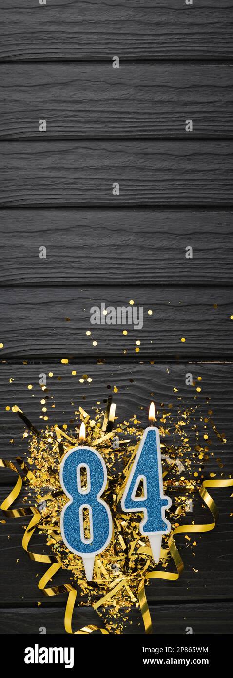Number 84 blue celebration candle and gold confetti on dark wooden ...