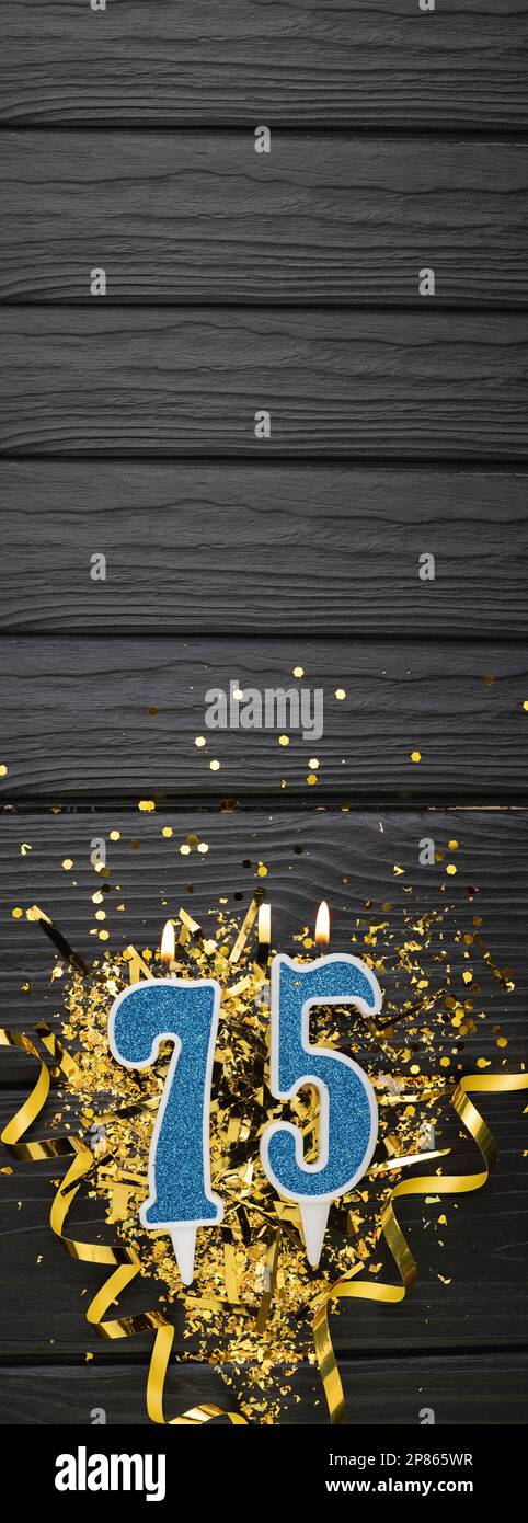 Number 75 blue celebration candle and gold confetti on dark wooden ...