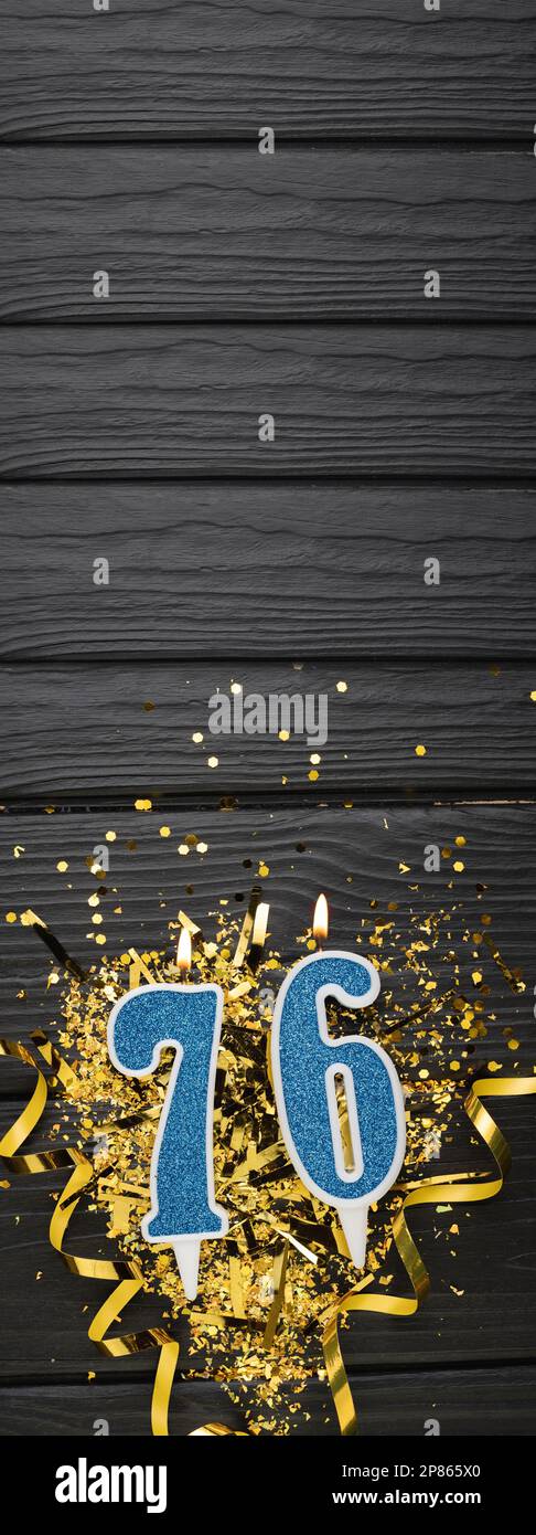 Number 76 blue celebration candle and gold confetti on dark wooden ...